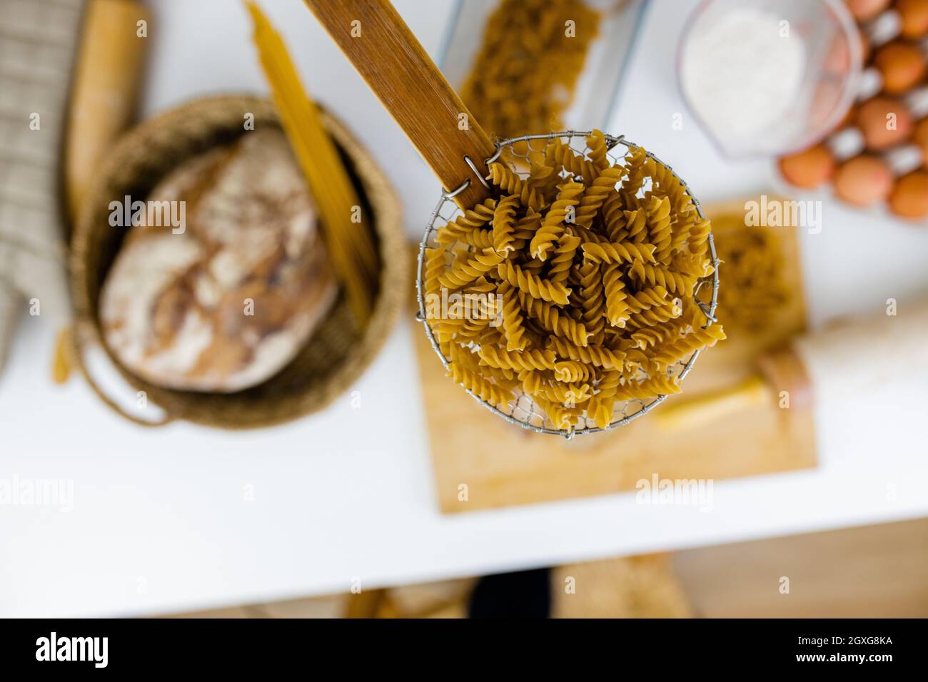 Uncooked fusilli on wooden pasta strainer above blurry ingredients on ...