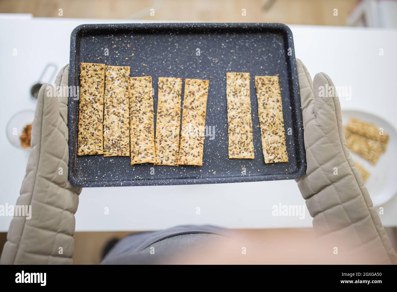 Gloved hands holding black tray of Swedish multi-seed crispbread above ...