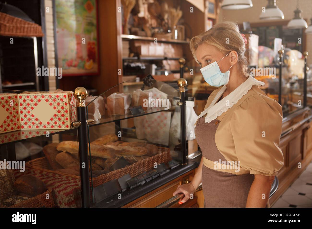 Professional female baker working at her bread shop, wearing medical ...