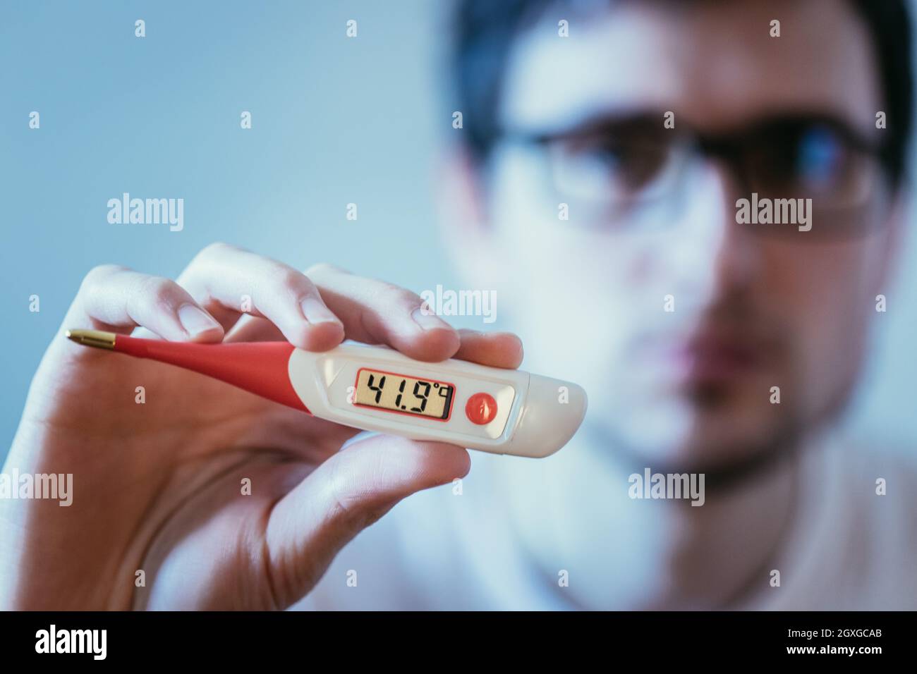 Man holds a red fever thermometer with high temperature in his hand ...
