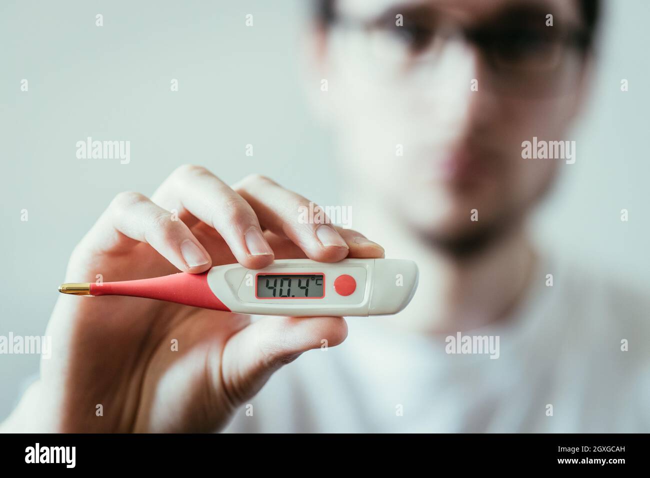 Man holds a red fever thermometer with high temperature in his hand ...