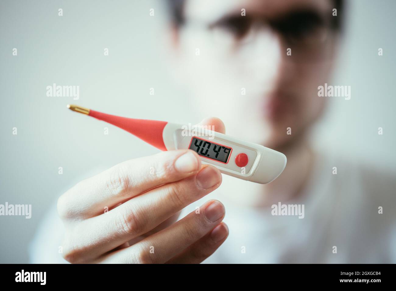 Man holds a red fever thermometer with high temperature in his hand ...