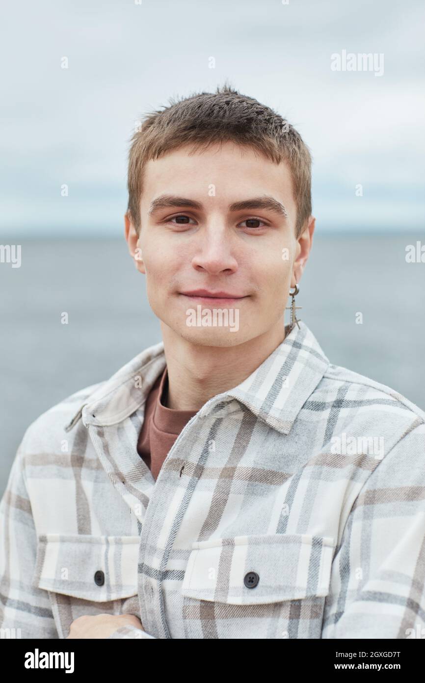 Vertical portrait of smiling young man looking at camera on beach with ...