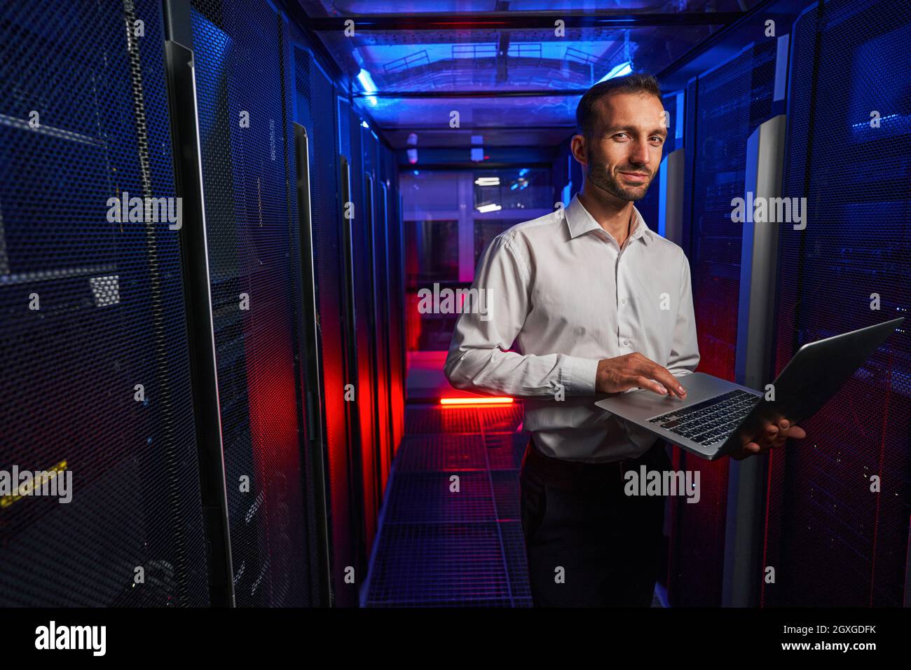 Bearded smiling it engineer in white shirt working with server rack and ...