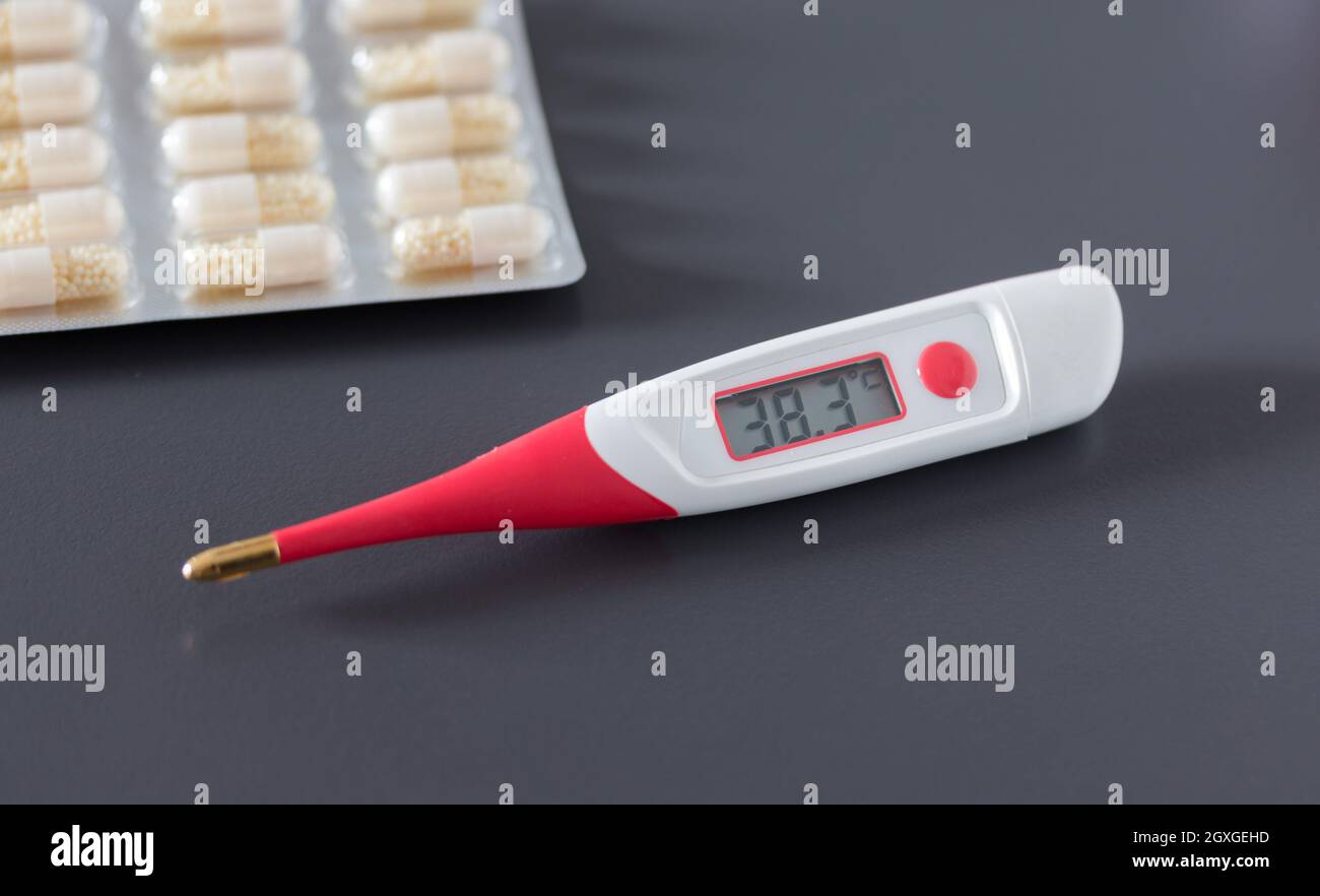 Red fever thermometer with digital display and pills lying on the desk ...