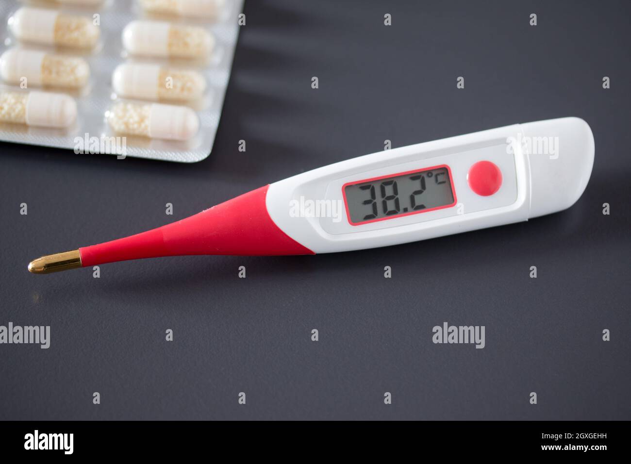 Red fever thermometer with digital display and pills lying on the desk ...