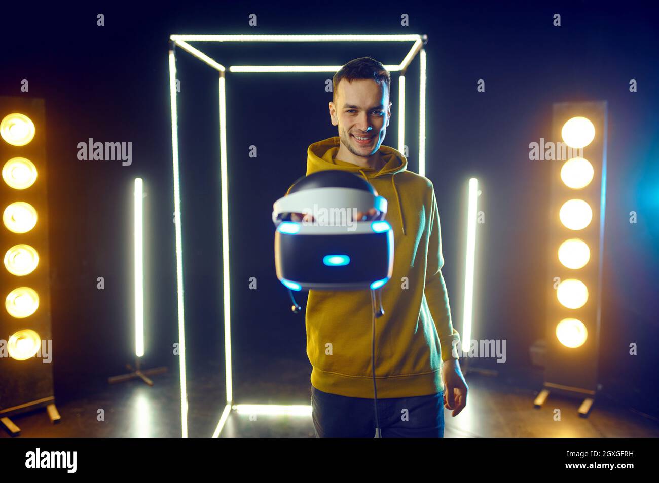 Young gamer poses with virtual reality headset and gamepad in luminous ...