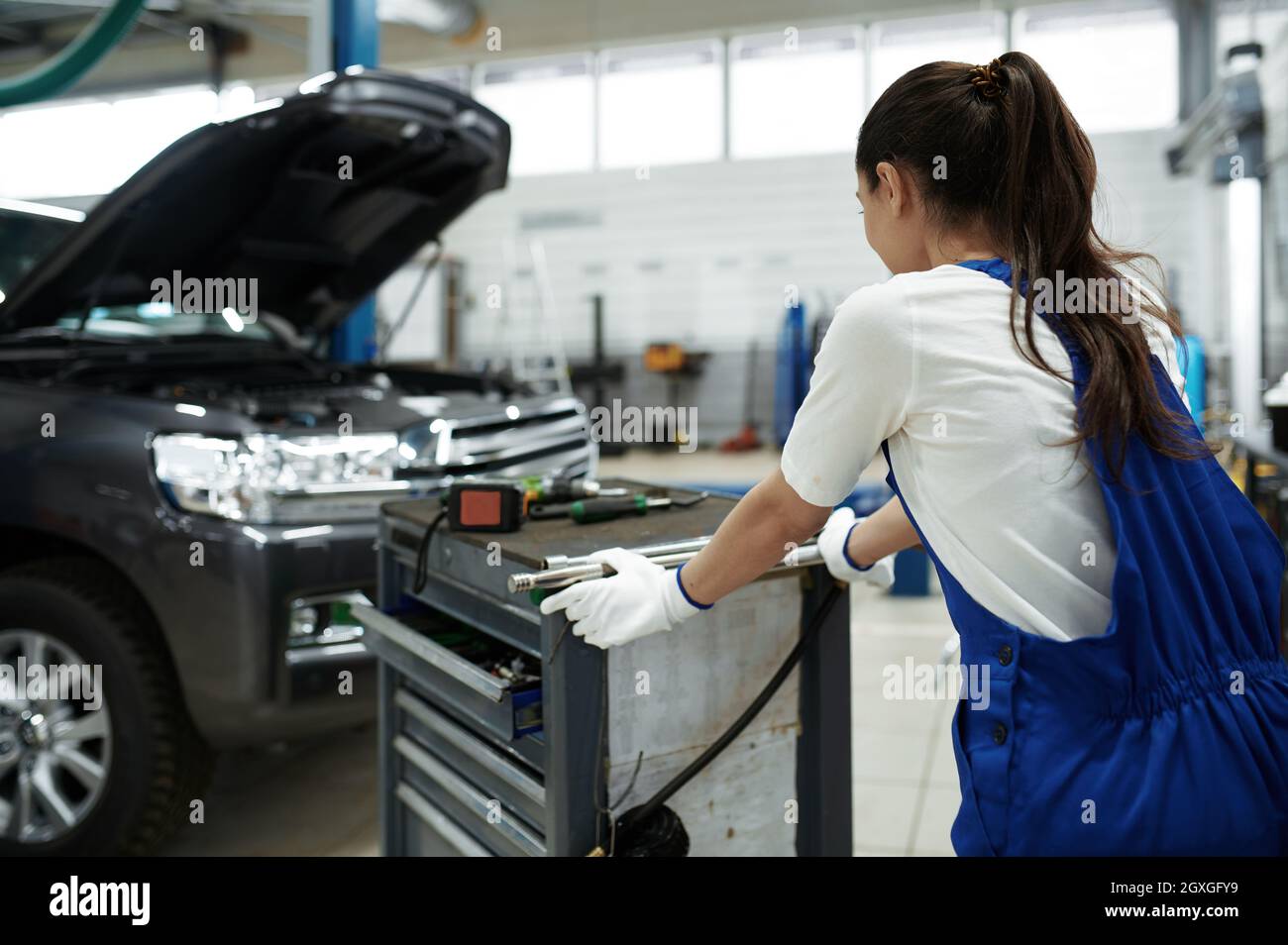 Female worker stands at the hood, car service. Vehicle repairing garage ...