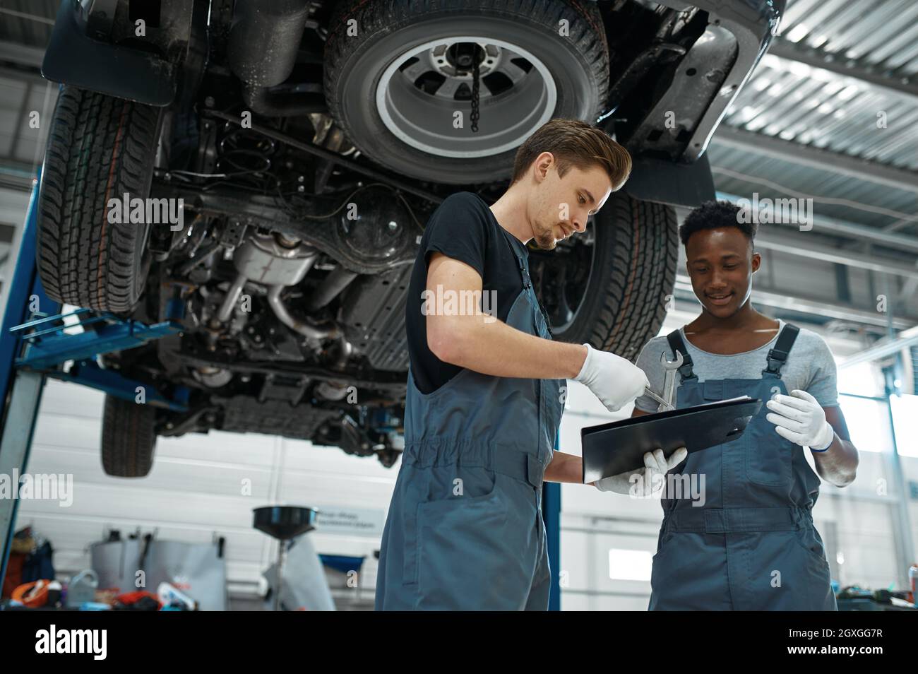 Two male mechanics looking on checklist, car service. Vehicle repairing ...