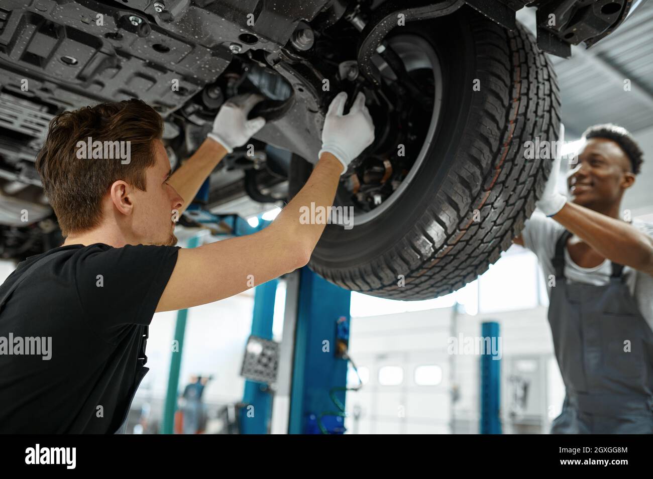 Two male workers fixes wheel, car service. Vehicle repairing garage ...