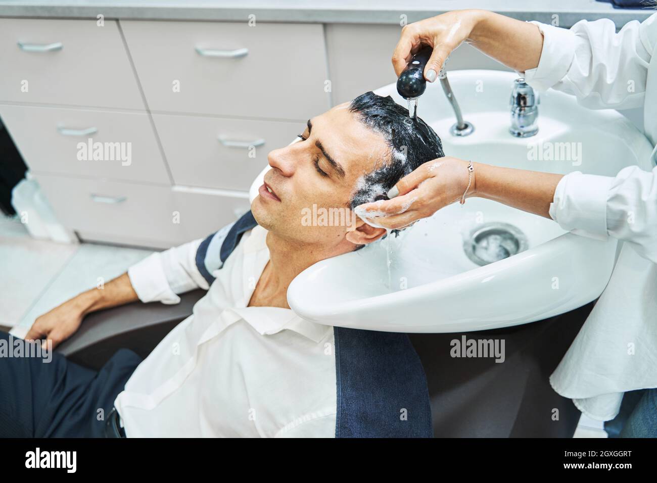 Barber spraying water on hair of relaxed client Stock Photo - Alamy