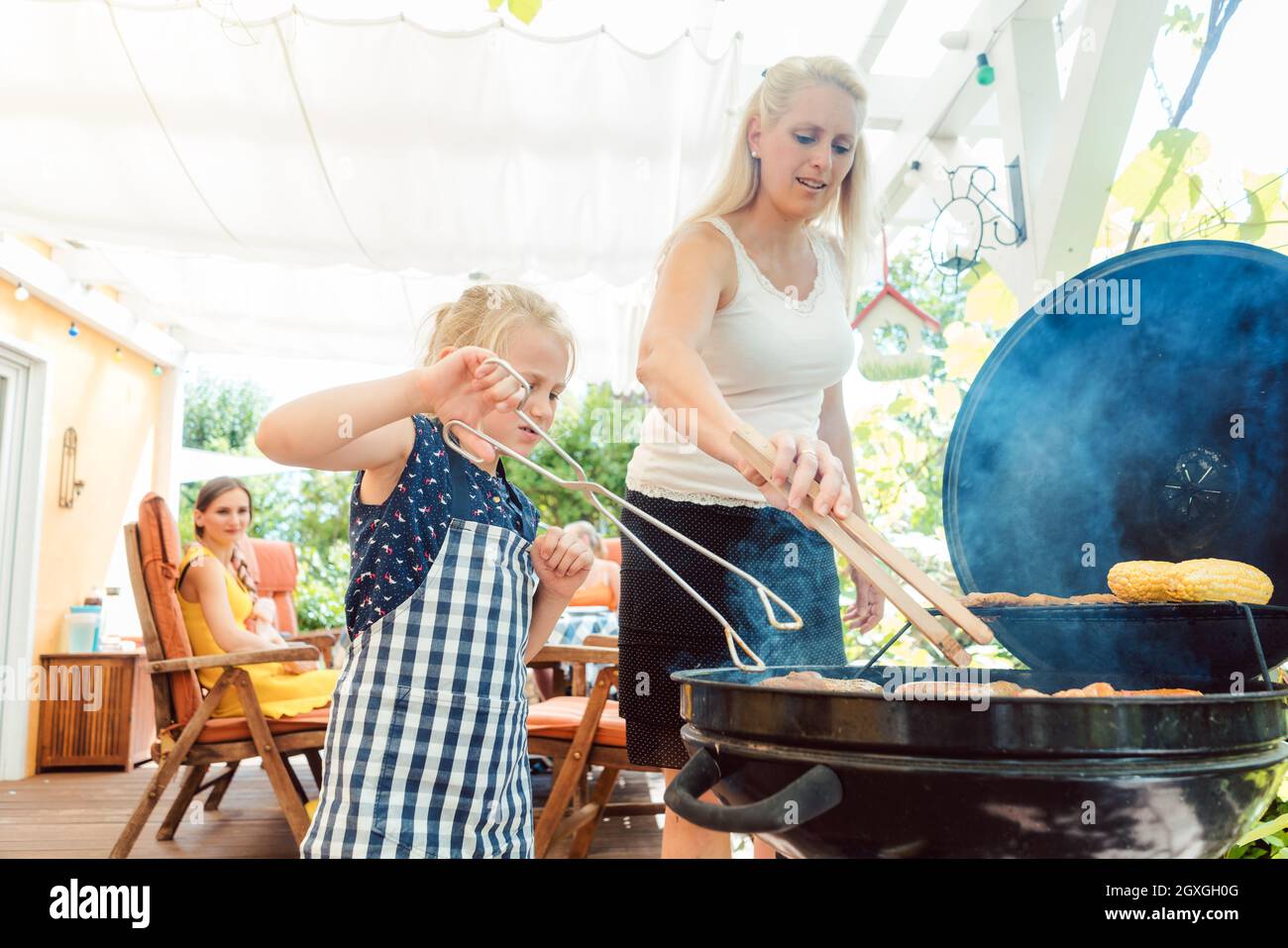 Mom and daughter at the grill doing the barbeque, while people are ...