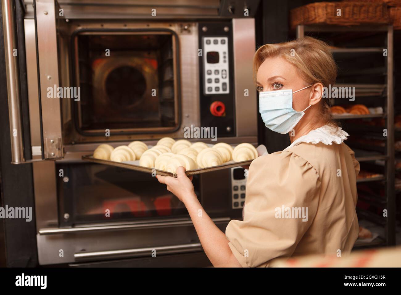 Professional baker wearing medical face mask while baking croissants at ...