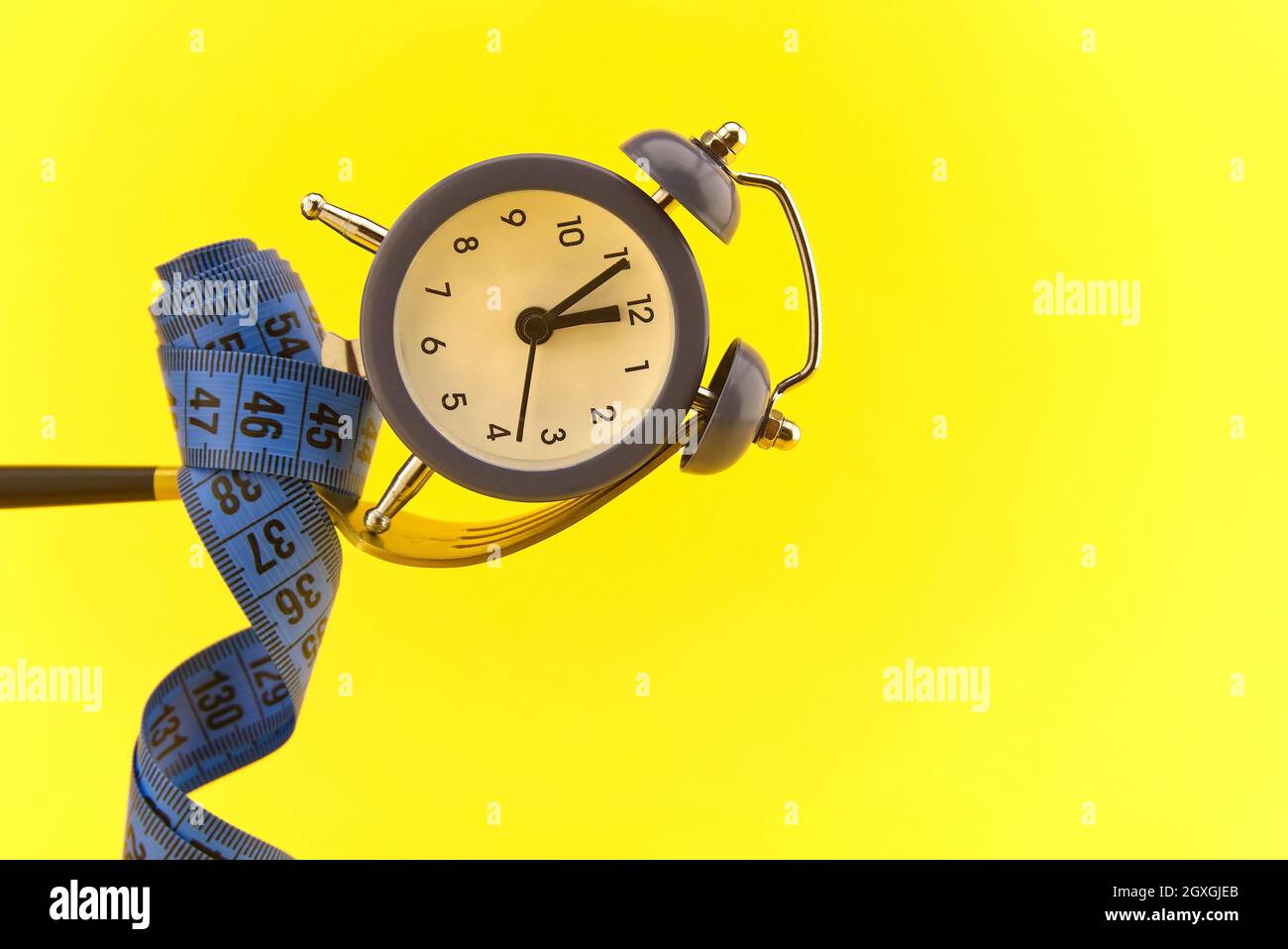 Alarm clock on golden fork wrapped with measuring tape above yellow ...