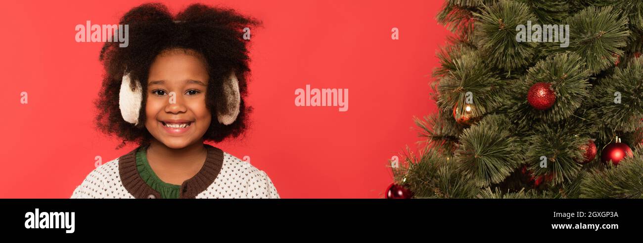 African american girl in ear muffs smiling at camera near christmas ...