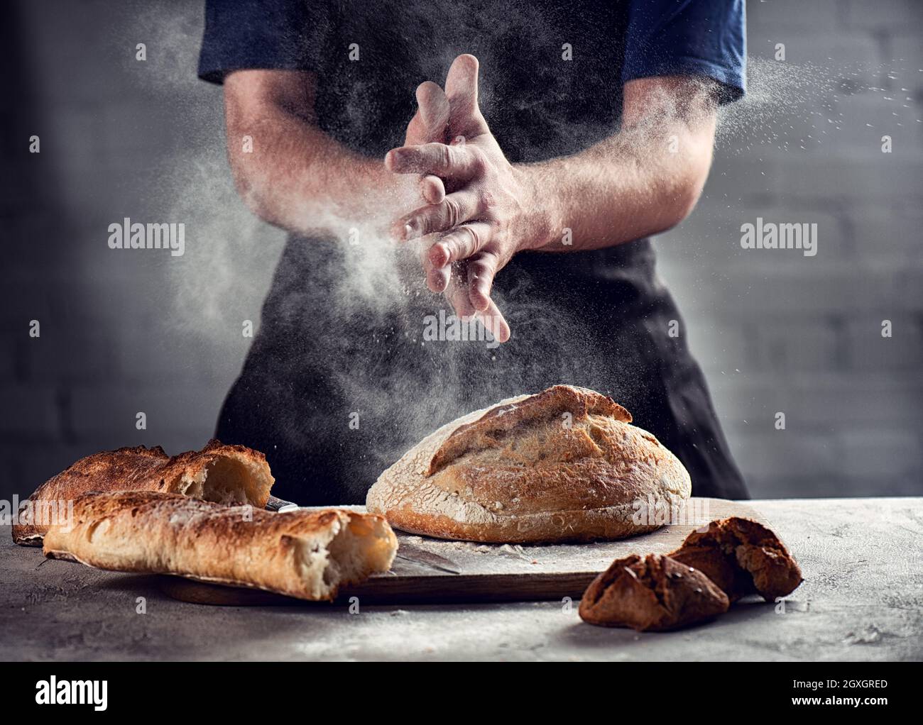 Chef sprinkles fresh bread with flour at the table in the kitchen Stock ...