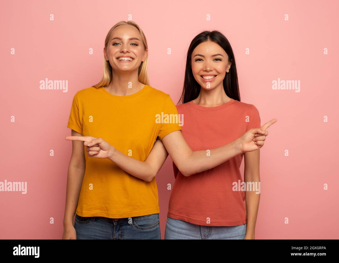 Two girls indicates something. Joyful and happy expression face. Pink ...