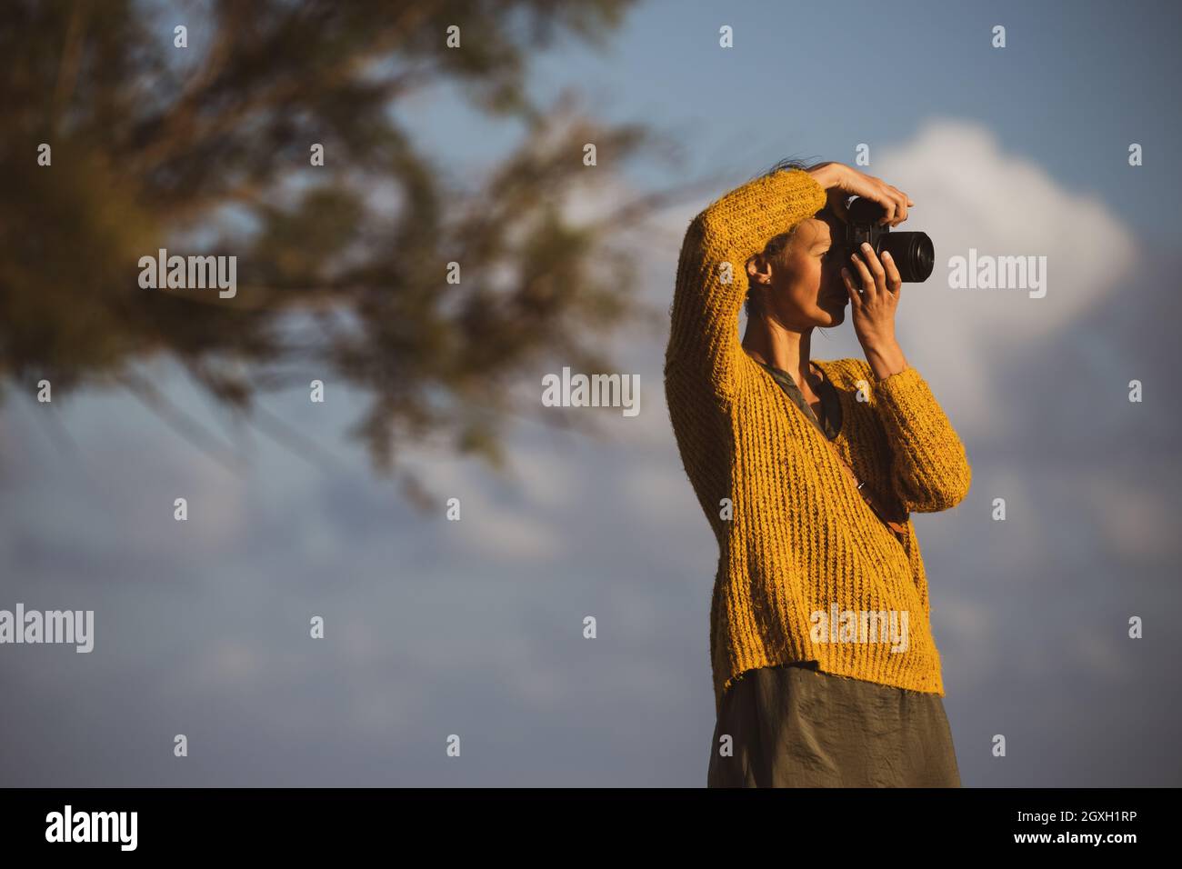 Pretty, young woman with a mirrorless camera, taking photos by the sea ...