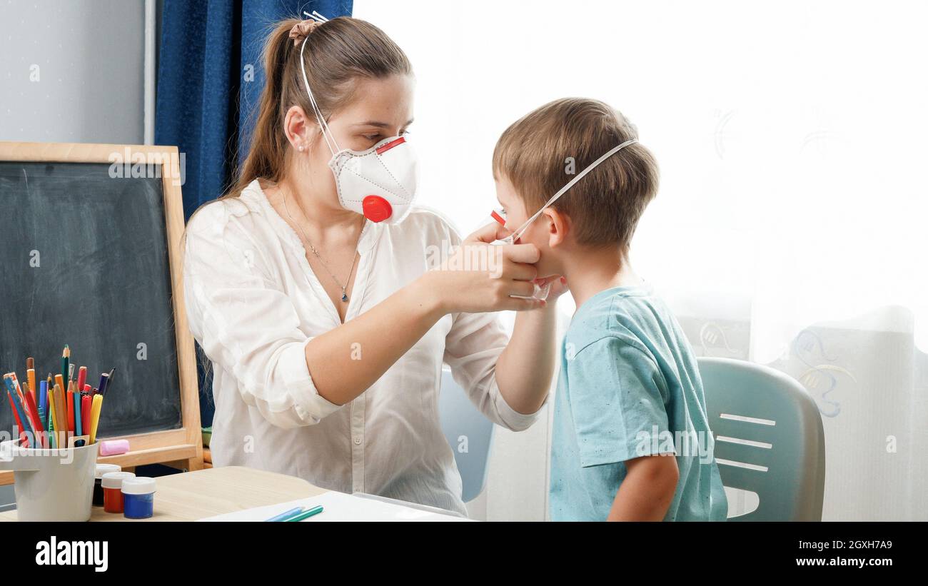 Young female teacher and little boy wearing protective mask respirators ...