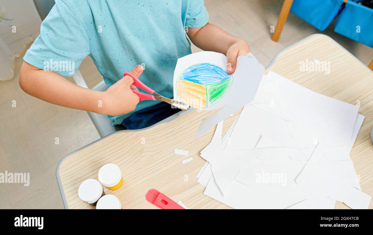 Closeup of little smart boy cutting out drawn picture with scissors ...
