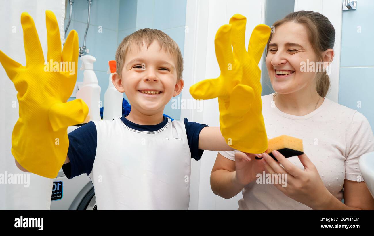 SMiling toddler boy wearing yellow rubber gloves laughing while doing ...