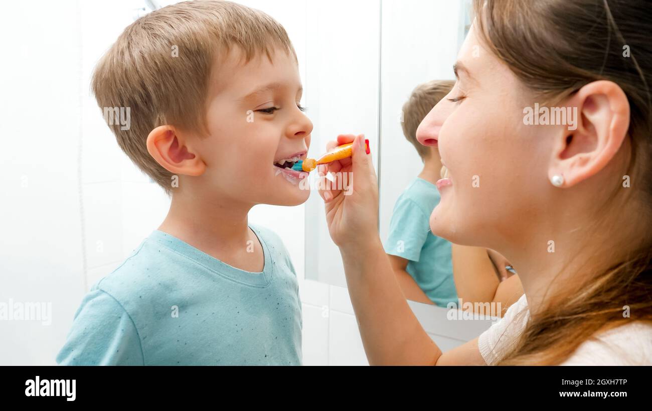 Young caring mother brushing and cleaning teeth of her little son ...