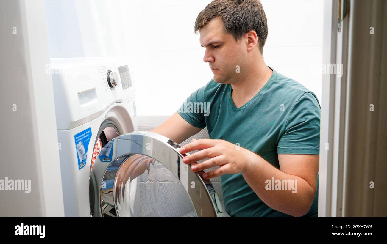 Young handsome man loading dirty clothes in washing machine and doing ...