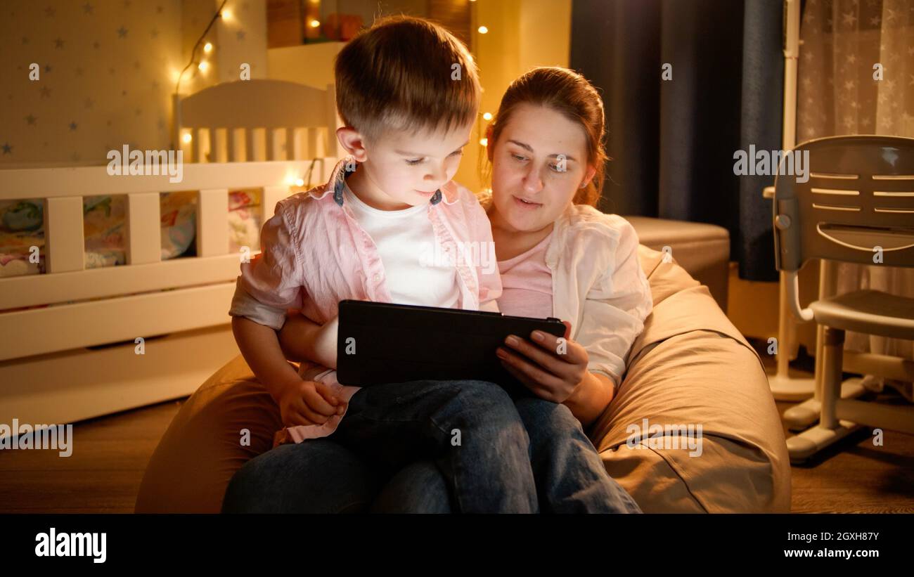 Portrait of little boy sitting on mothers lap and watching cartoons on ...