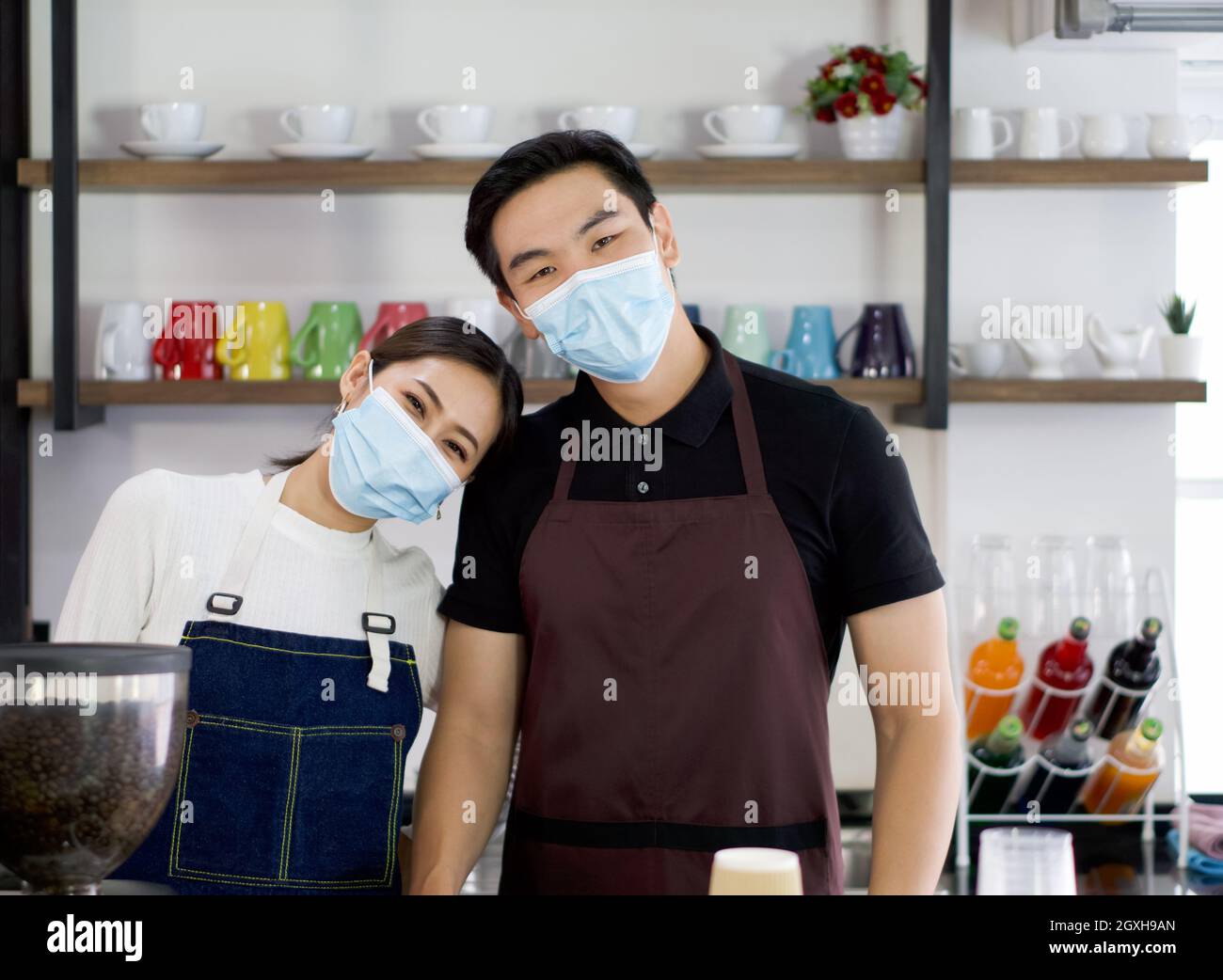 The shopkeeper and barista, wearing a face mask, poses happily before ...