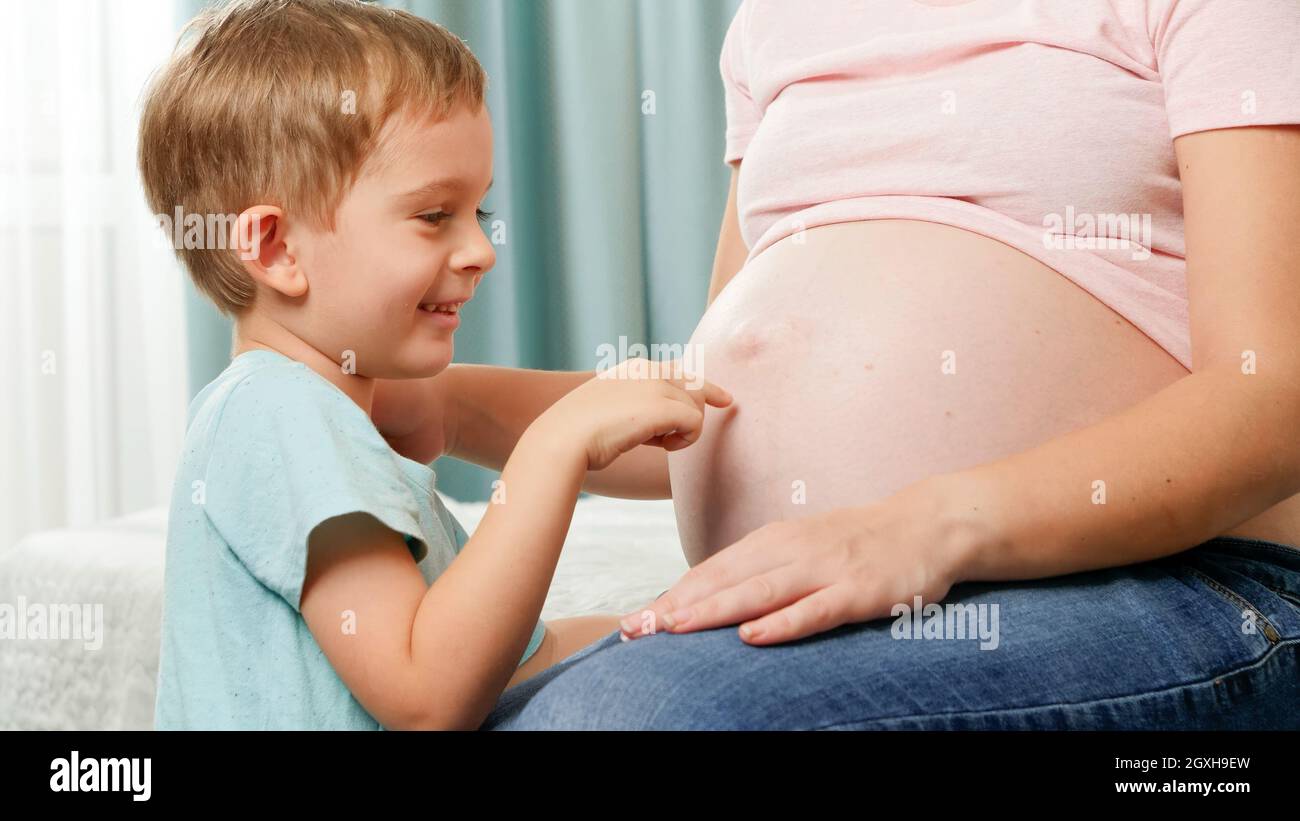 Smiling happy little boy tickling and having fun with big pregnant ...