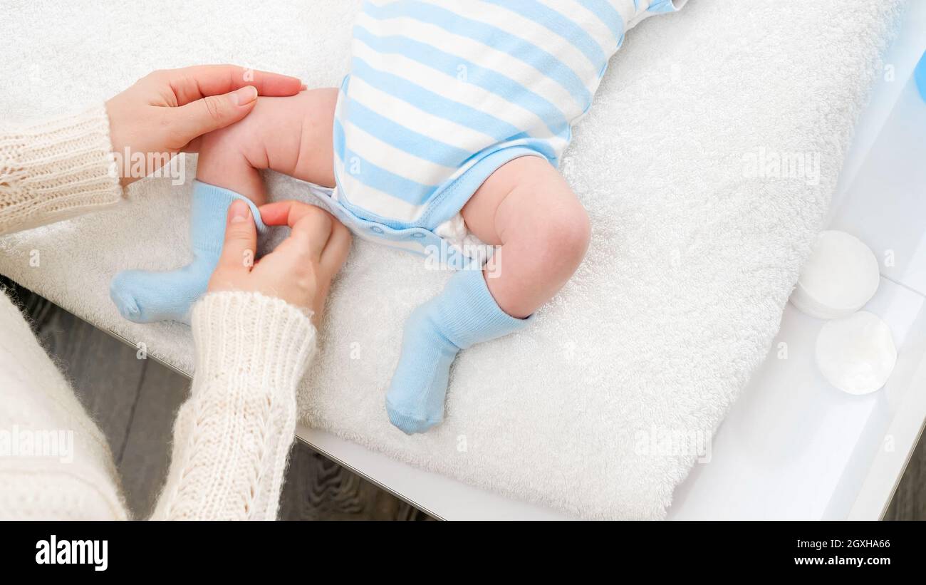 Closeup of young mother dressing her little baby son in socks while ...