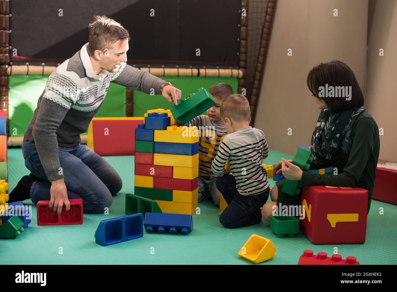 young happy parents having fun with kids in children playground indoor ...