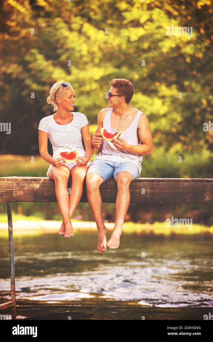 couple in love enjoying watermelon while sitting on the wooden bridge ...