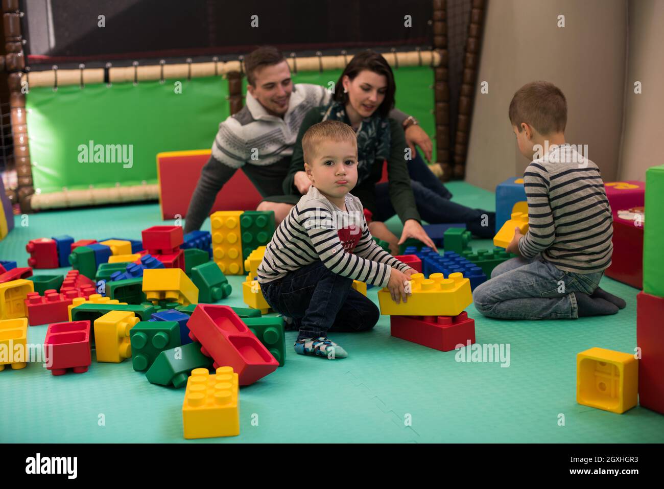 young happy parents having fun with kids in children playground indoor ...