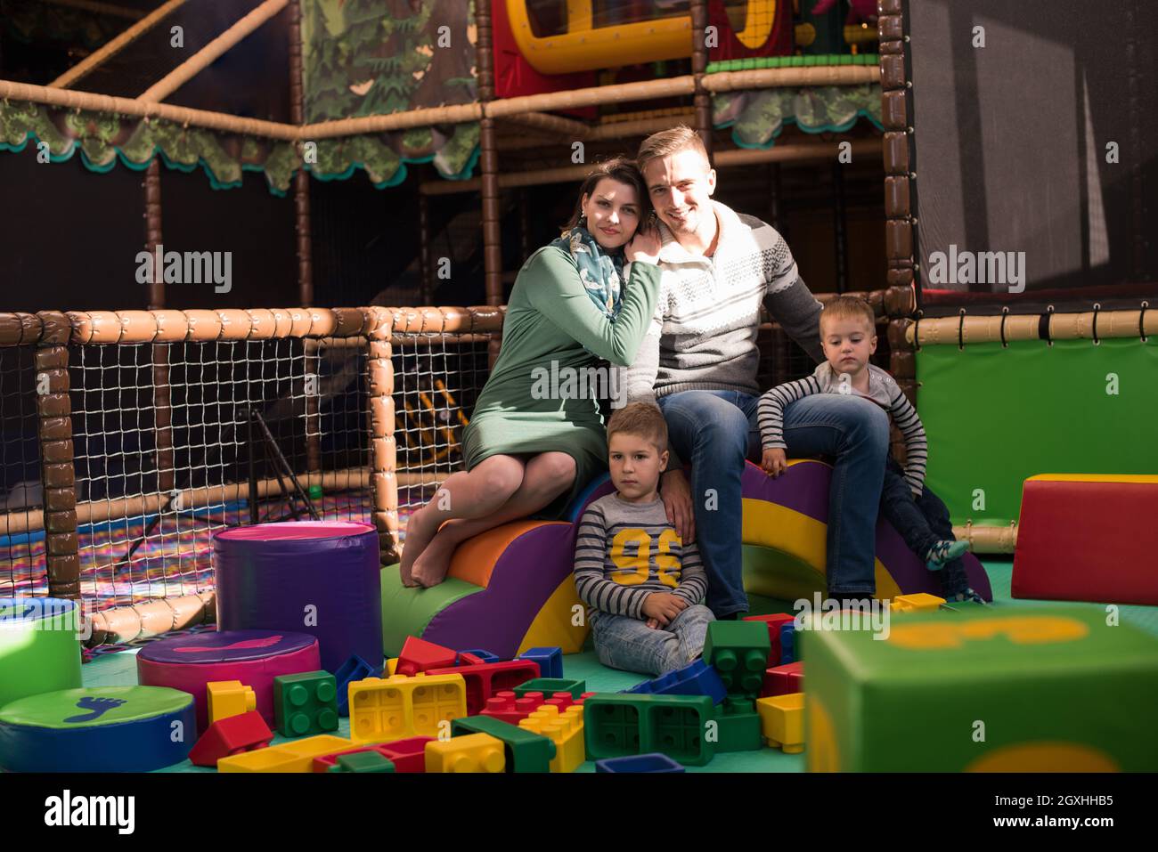 young happy parents having fun with kids in children playground indoor ...