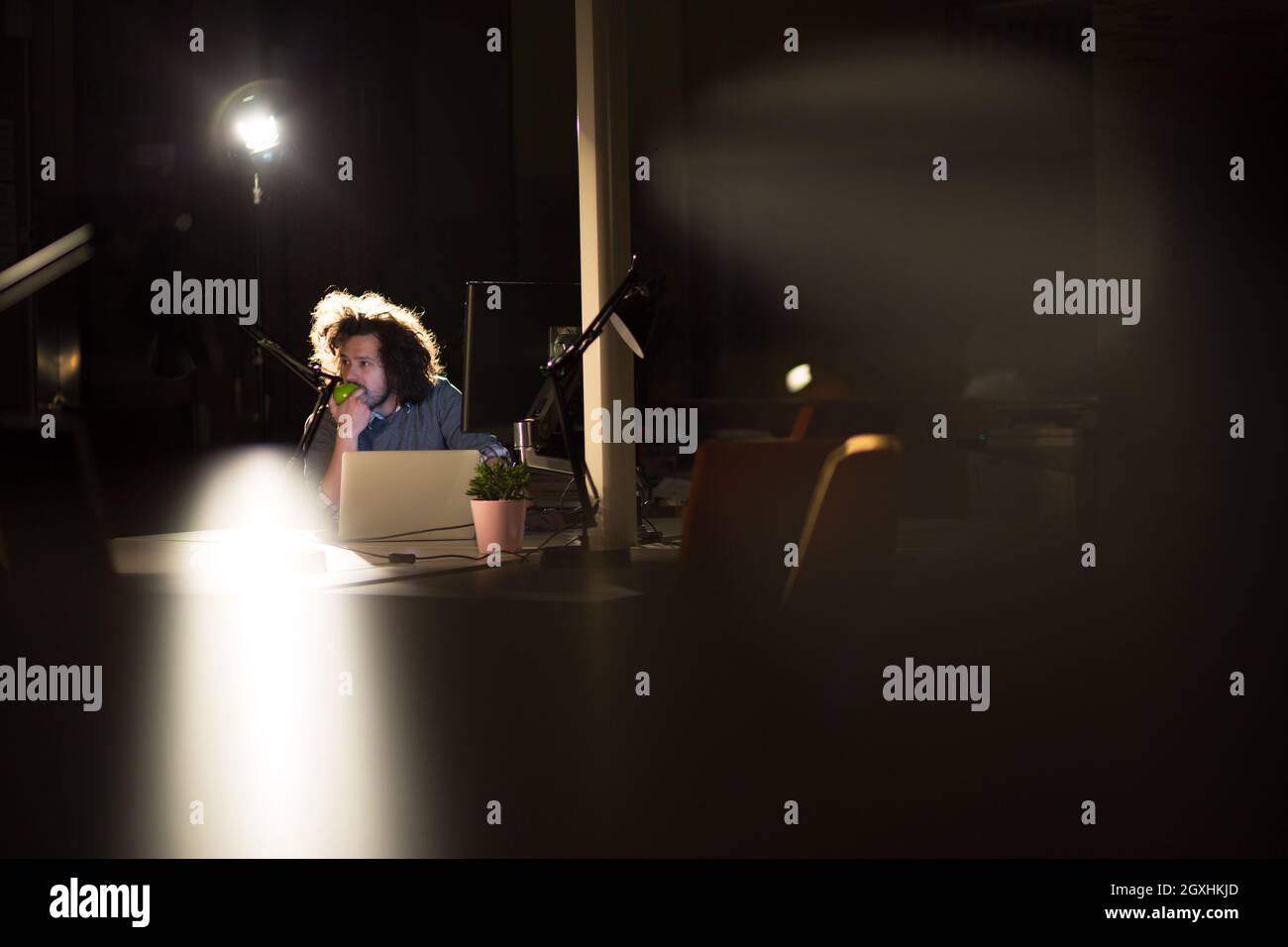 Young man working on computer at night in dark office. The designer ...