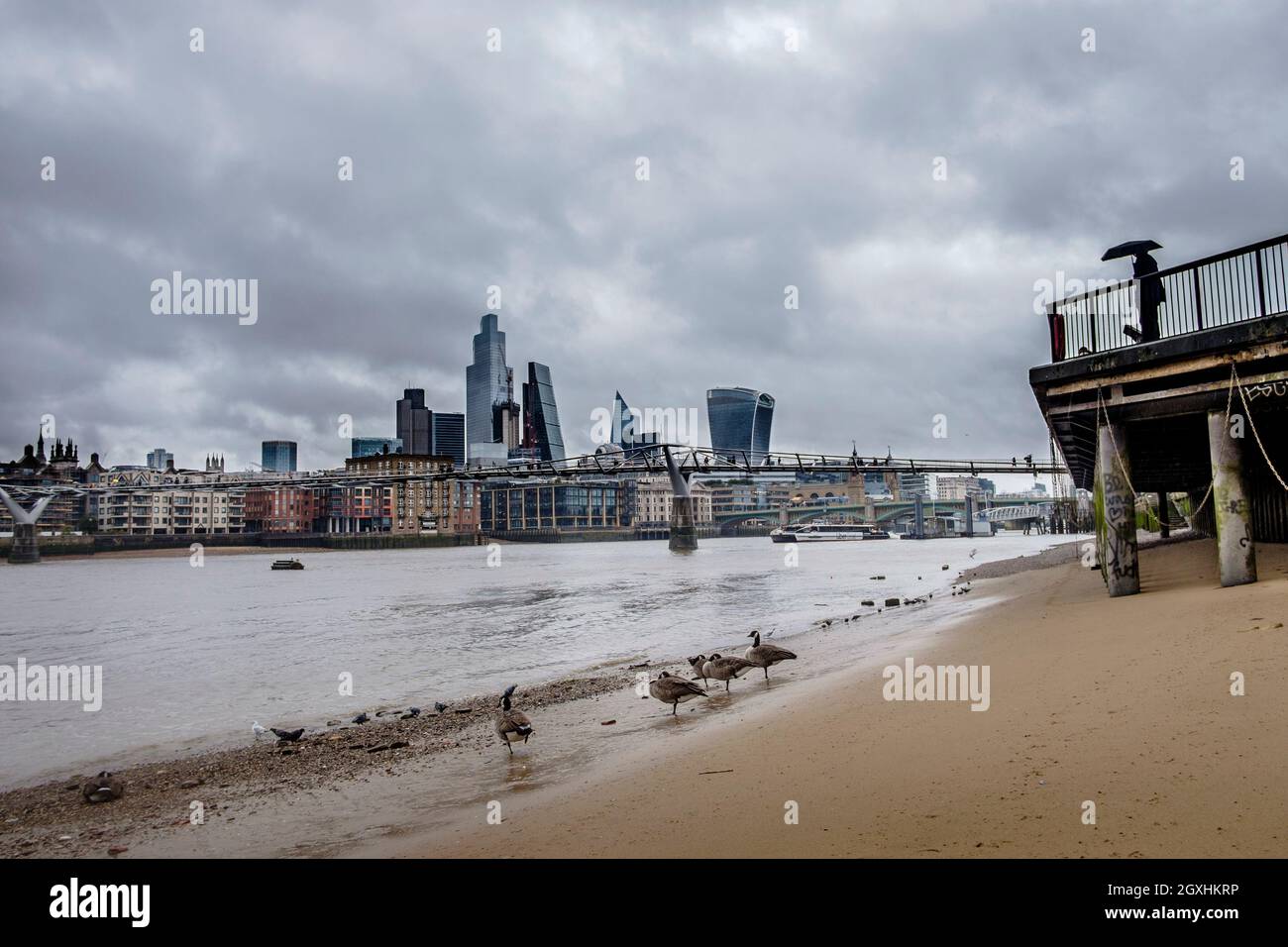 River Thames at low tide with stormy skies over the City of London ...