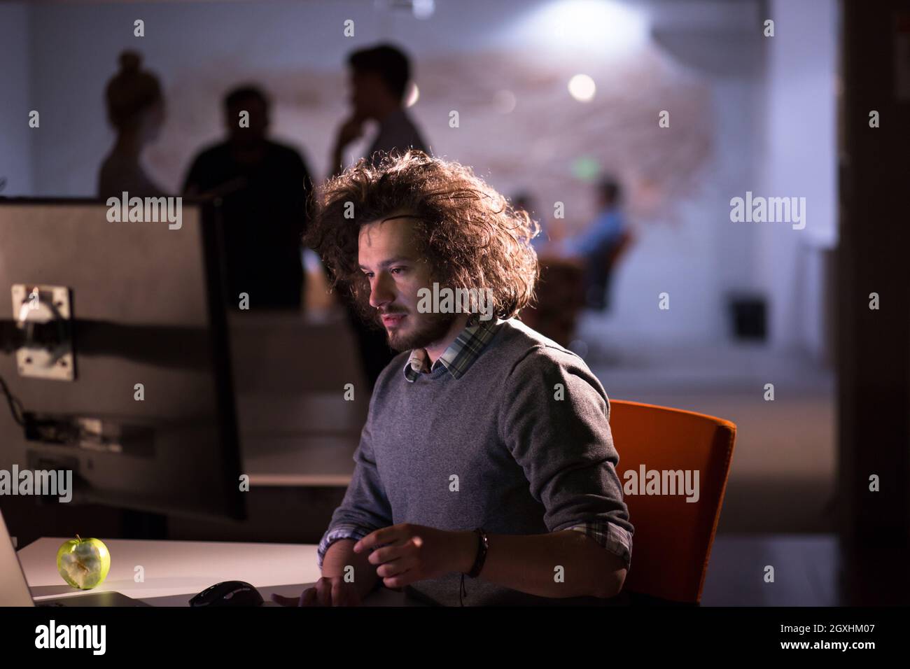 Young man working on computer at night in dark office. The designer ...