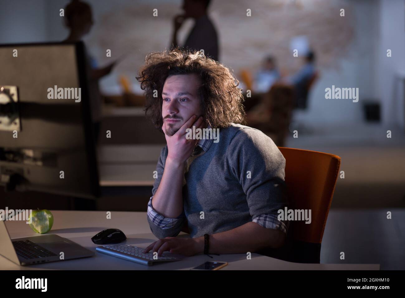 Young man working on computer at night in dark office. The designer ...