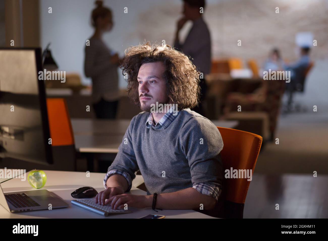 Young man working on computer at night in dark office. The designer ...