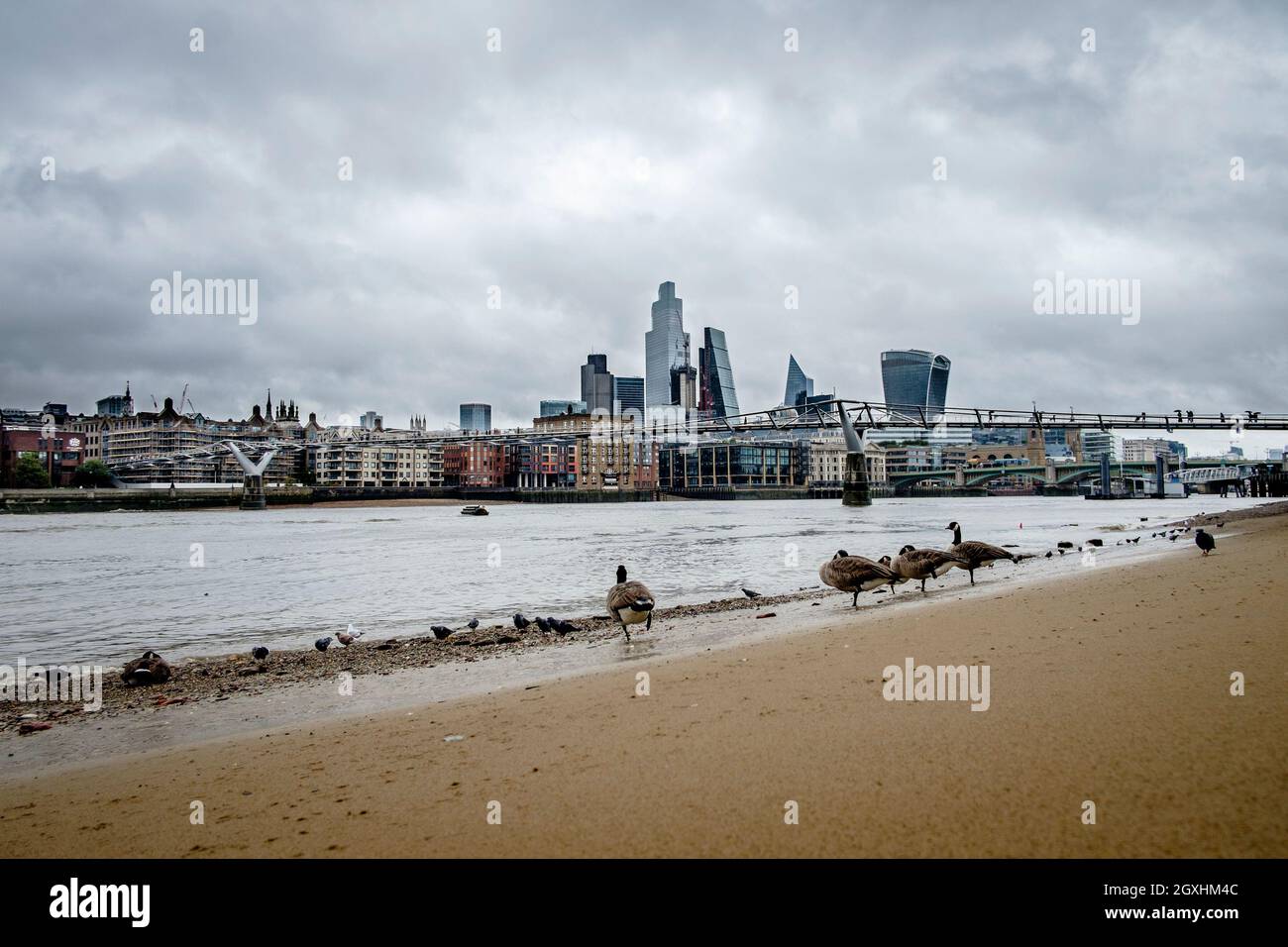 River Thames at low tide with stormy skies over the City of London ...