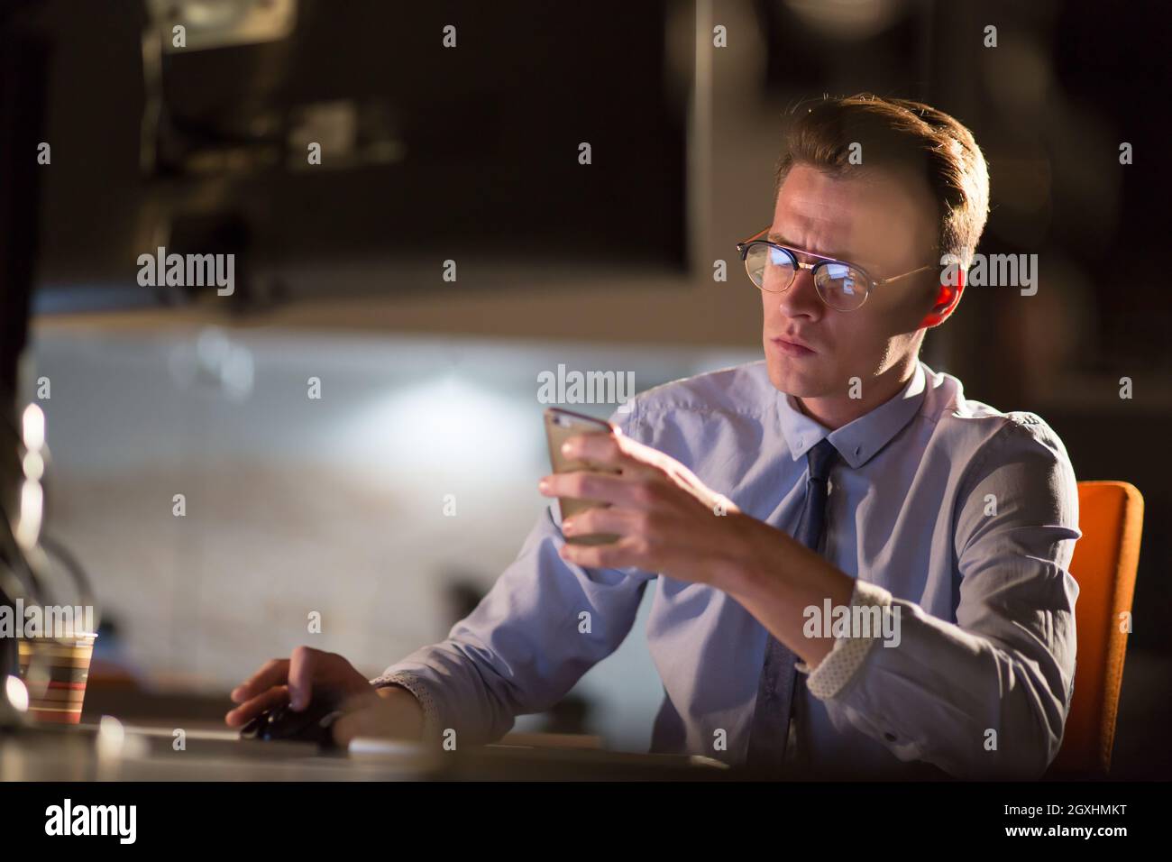 Young man using mobile phone while working on computer at night in dark ...