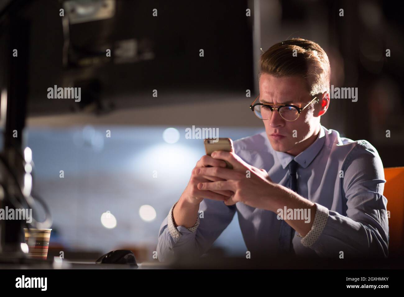 Young man using mobile phone while working on computer at night in dark ...