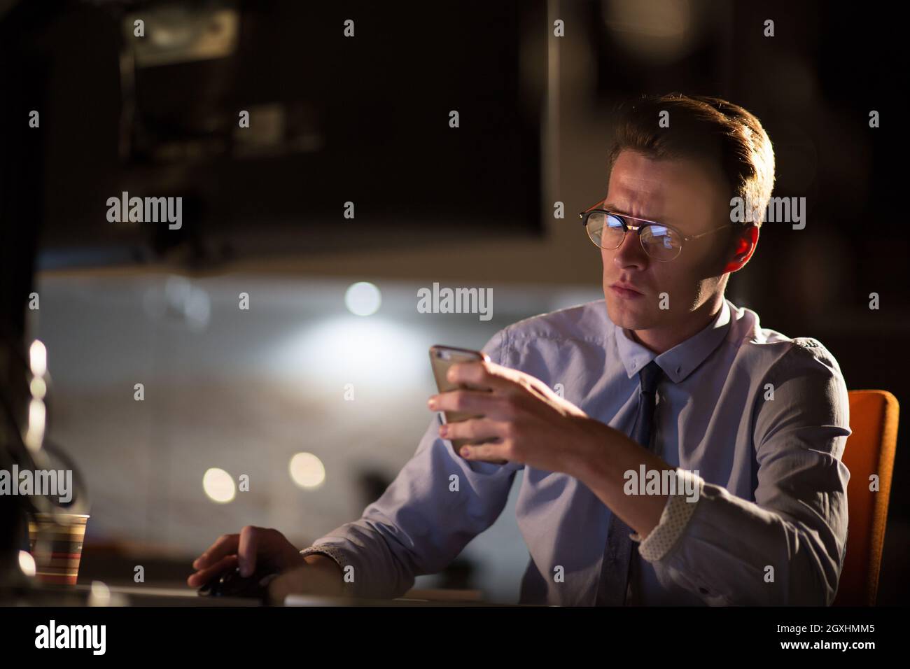 Young man using mobile phone while working on computer at night in dark ...