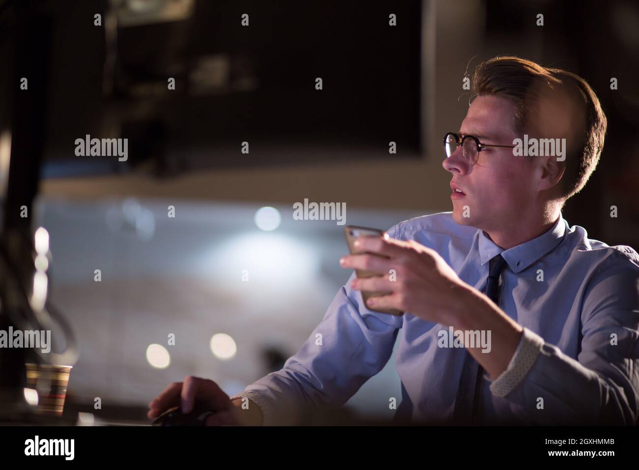 Young man using mobile phone while working on computer at night in dark ...