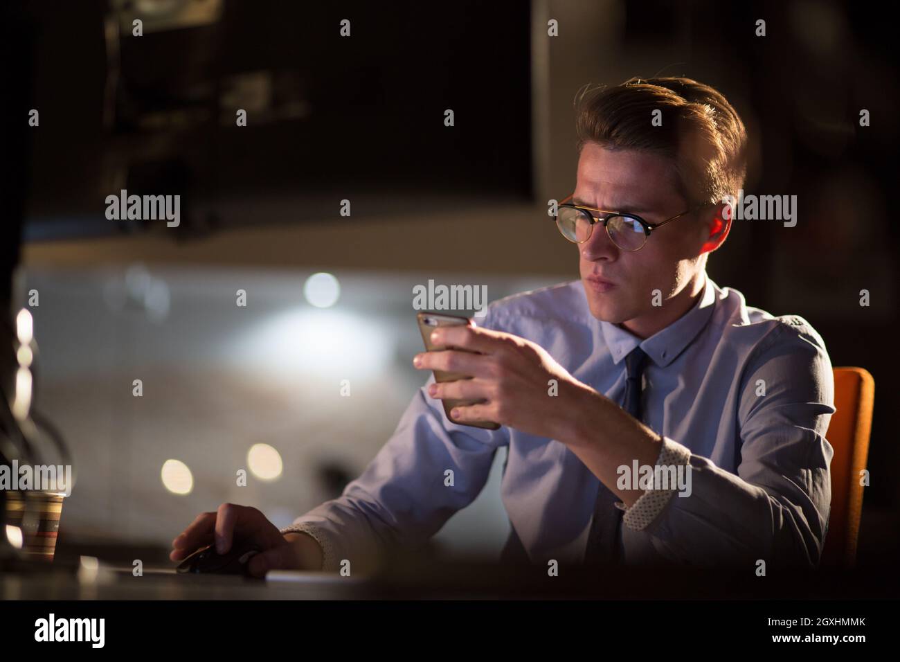 Young man using mobile phone while working on computer at night in dark ...