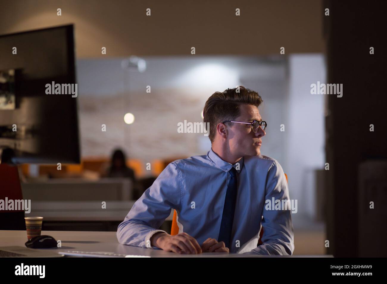Young man working on computer at night in dark office. The designer ...