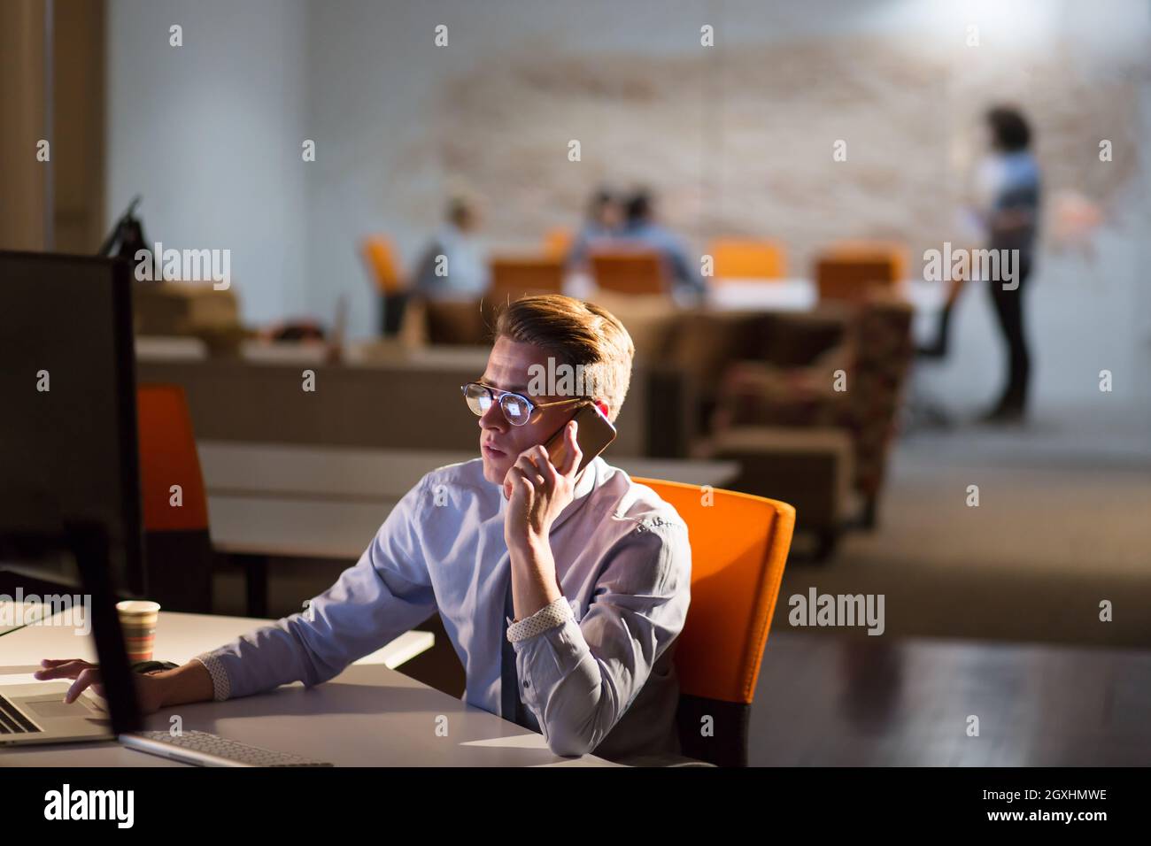 Young man using mobile phone while working on computer at night in dark ...