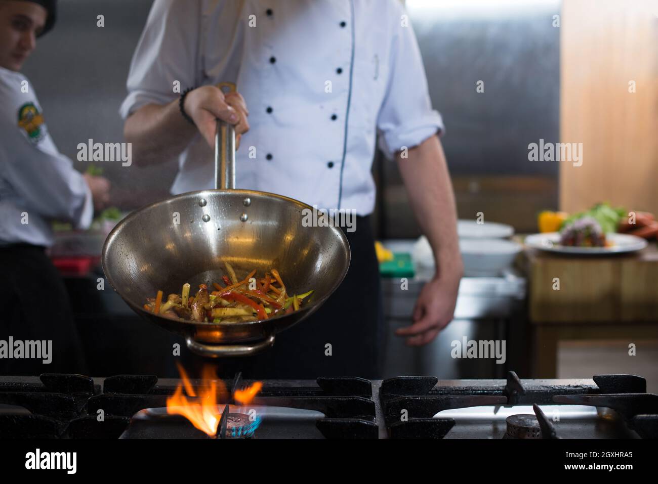 Young male chef flipping vegetables in wok at commercial kitchen Stock ...