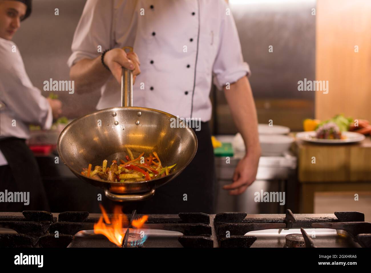 Young male chef flipping vegetables in wok at commercial kitchen Stock ...